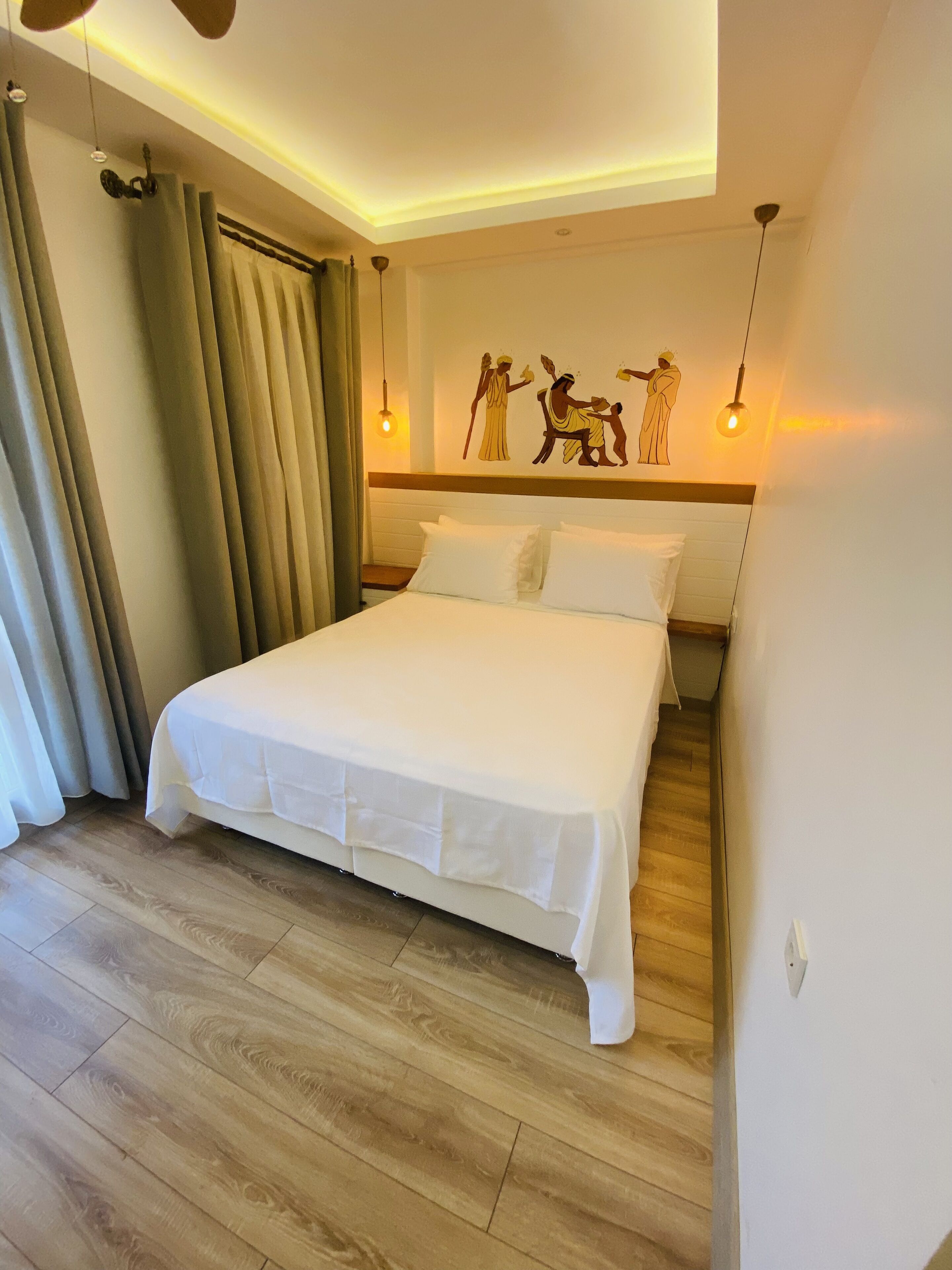 Cama bem arrumada em quarto de hotel, com piso de madeira, luminária no teto e parede com mural.