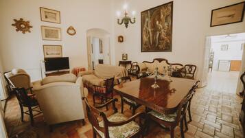 Uma área de refeições com mesa e cadeiras de madeira, um sofá, televisão e decorações nas paredes.