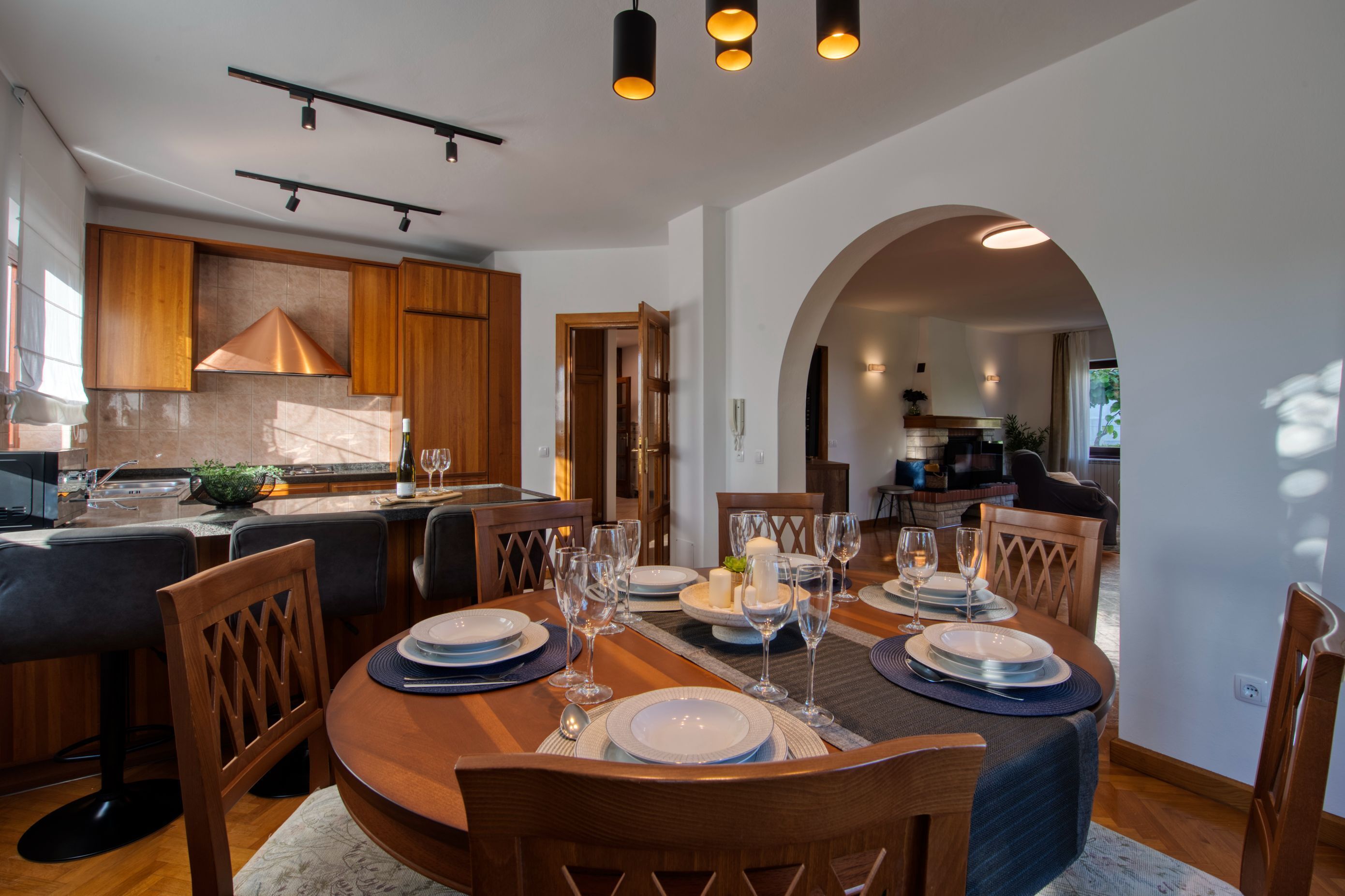Uma cozinha moderna com armários de madeira, uma ilha central e uma área de jantar com mesa redonda para seis pessoas.