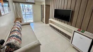 Uma sala de estar moderna com uma televisão de tela plana fixada em uma parede de madeira, um sofá com almofadas estampadas, uma mesa pequena e um mini-refrigerador.