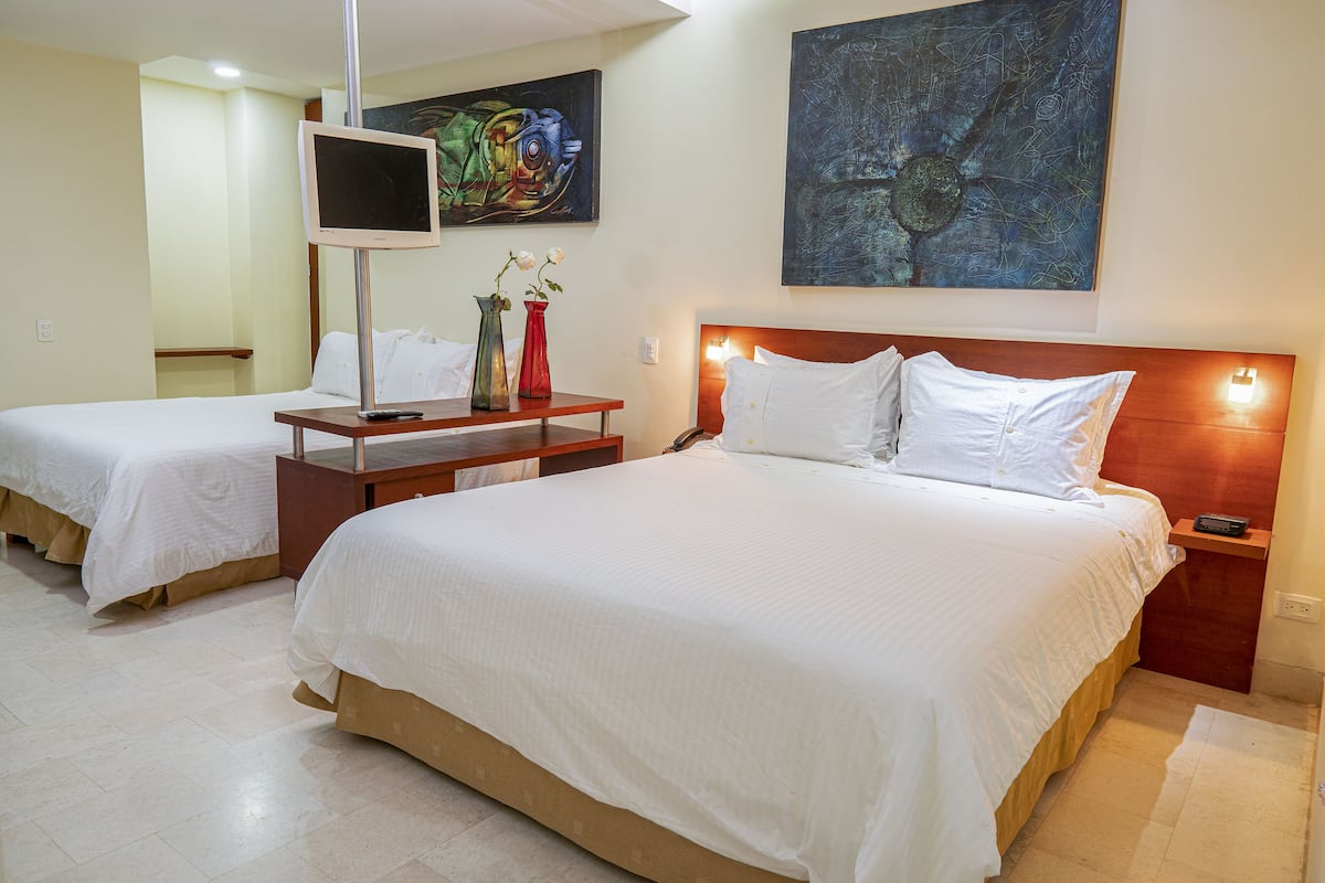 Quarto de hotel com duas camas, uma televisão, um quadro e uma mesinha de cabeceira.