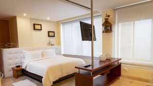 Quarto moderno com uma cama grande, mesas de cabeceira, TV na parede e janela com persianas.
