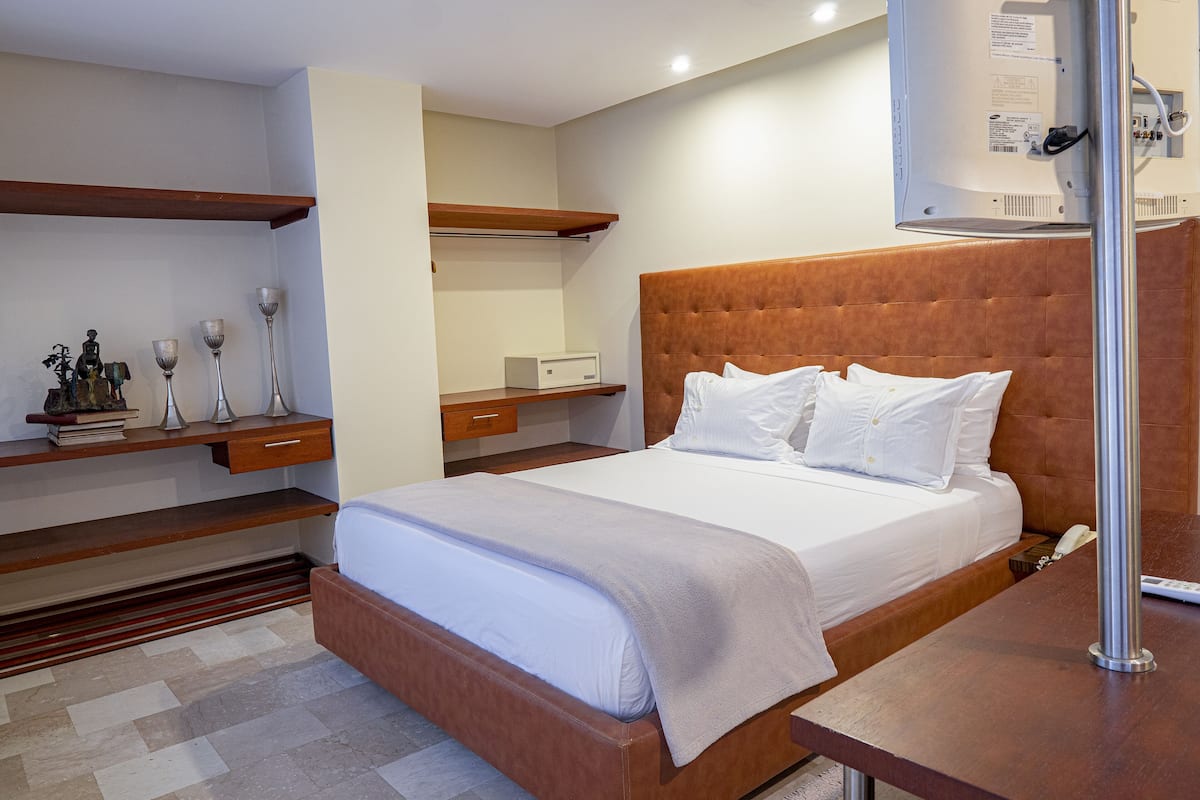Quarto de hotel moderno com uma cama grande, estantes embutidas e uma mesa de cabeceira.