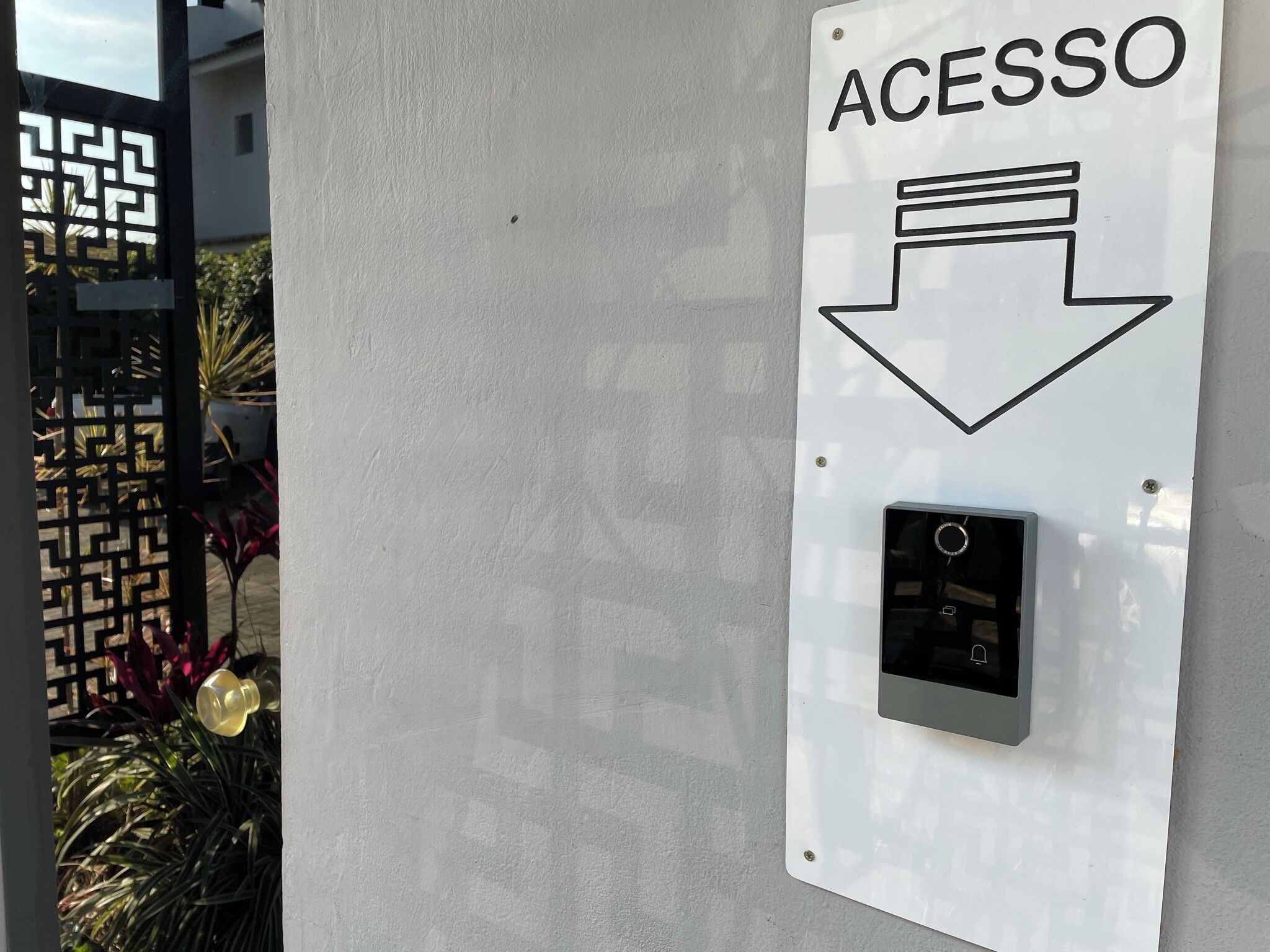 Sinal fixado na parede com a palavra 'ACESSO' e uma seta apontando para baixo, indicando uma entrada ou ponto de acesso, além de um teclado para controle de acesso.