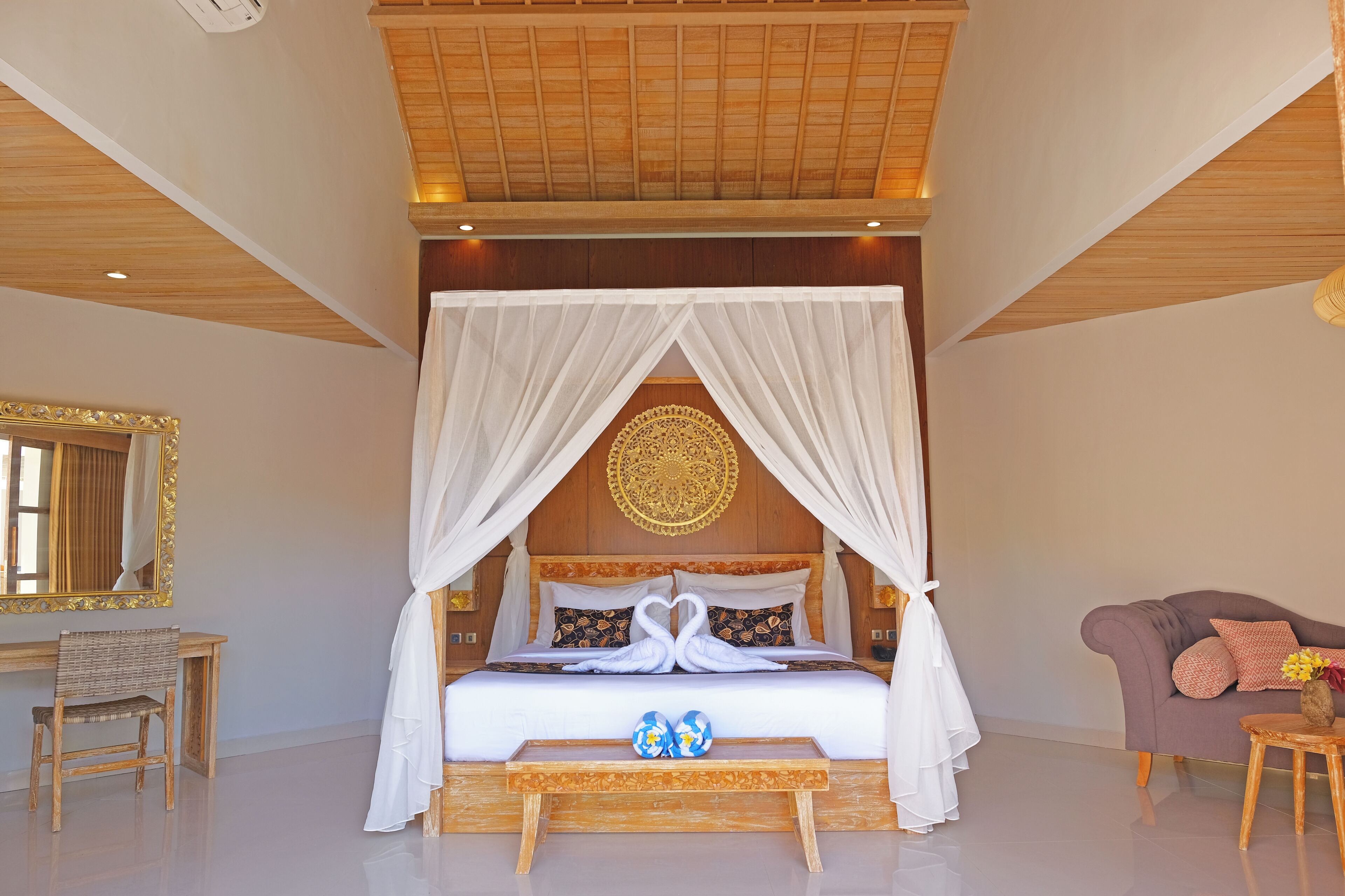 Quarto com cama de dossel, cabeceira de madeira, espelho, mesa de cabeceira e sofá.