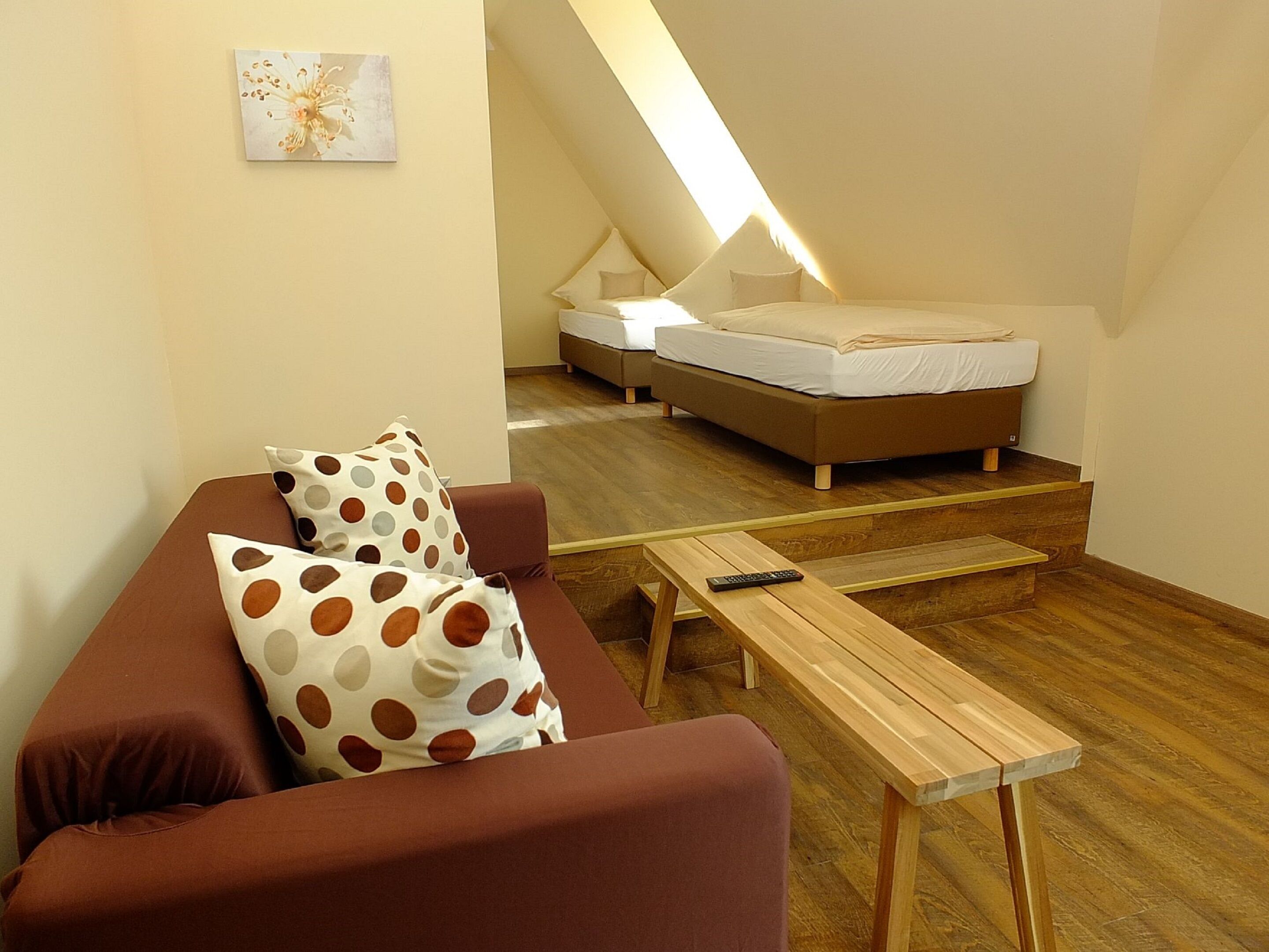 Quarto moderno e compacto com sofá marrom, mesa de centro de madeira e cama ao fundo.