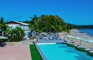 Área de piscina com espreguiçadeiras, piscina e vista para a praia.