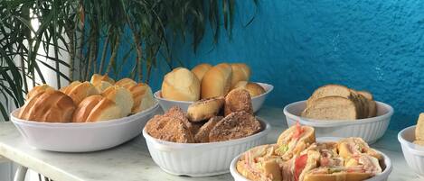 Uma mesa com diversos alimentos, incluindo pães, doces e uma salada.