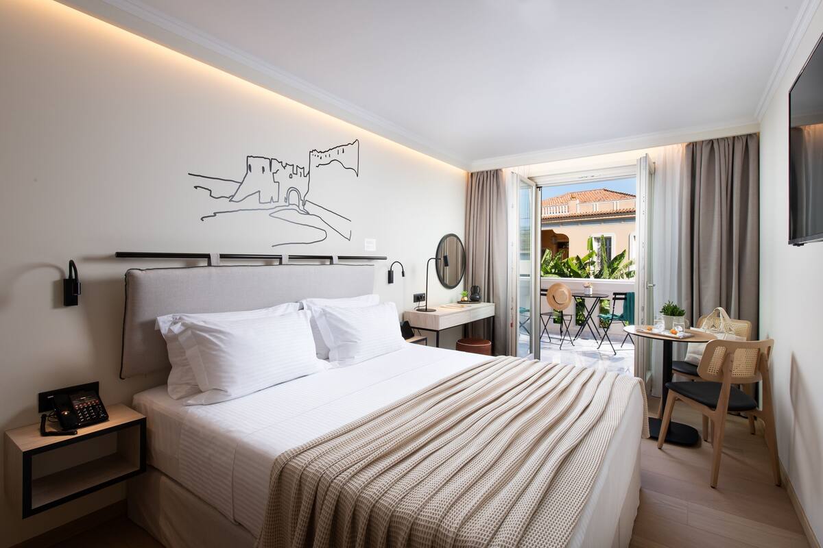 Quarto de hotel com cama, mesa de cabeceira e vista para a varanda.
