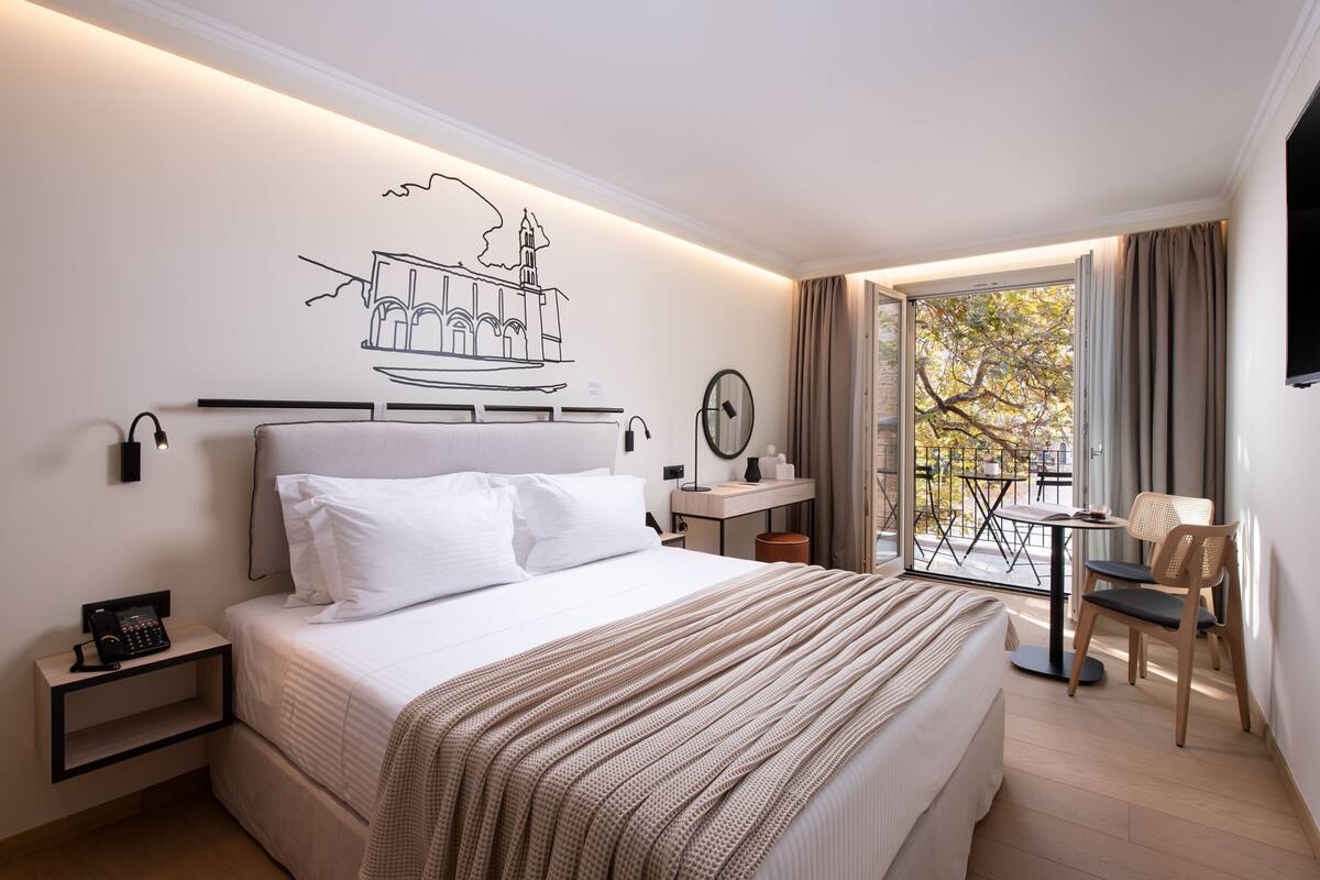 Quarto de hotel com cama, mesa de cabeceira, abajur e vista para o exterior.