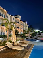 Área de piscina de hotel com espreguiçadeiras, guarda-sóis e piscina à noite.