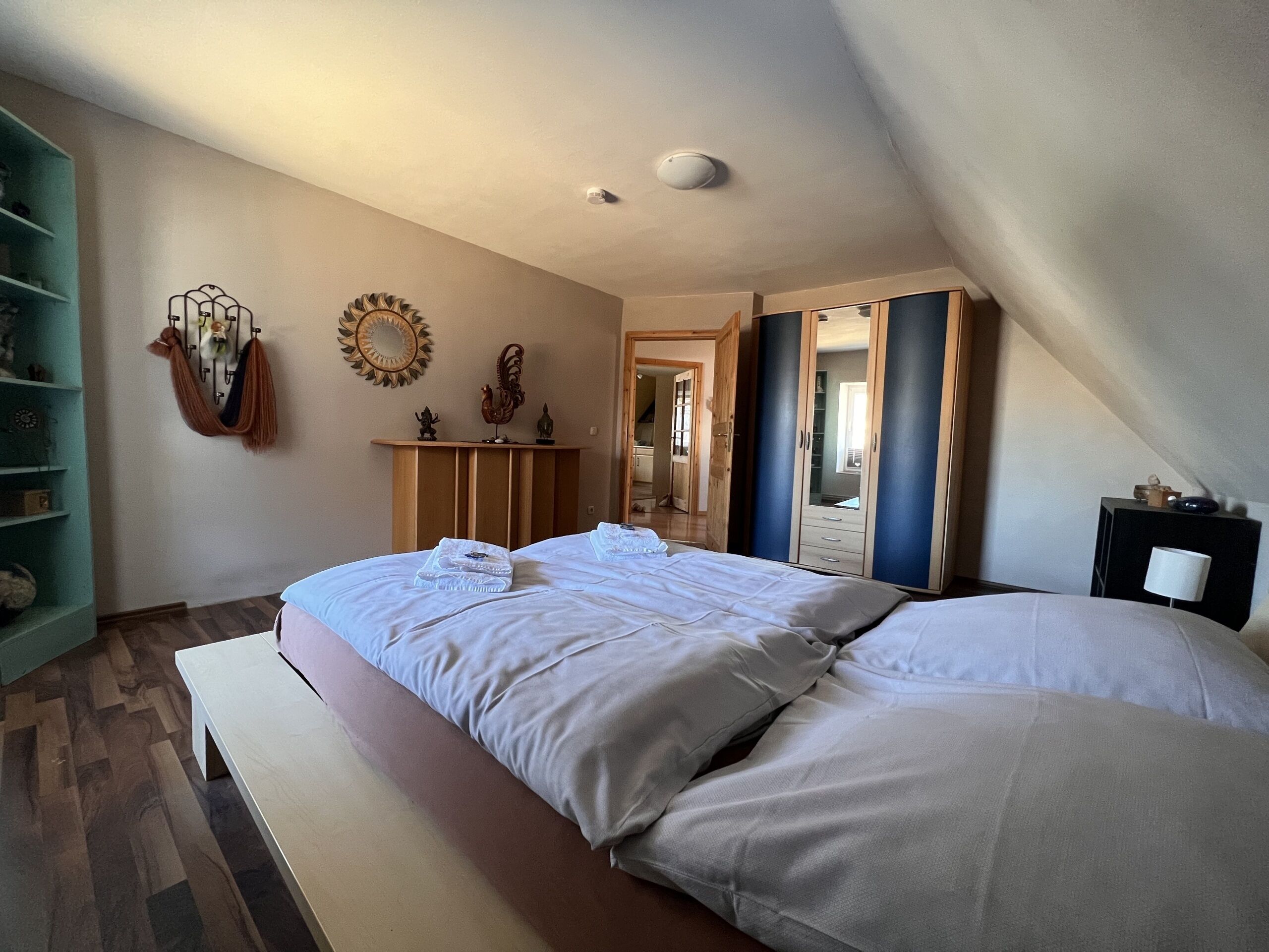 Quarto com uma cama grande, uma cômoda de madeira, um espelho e uma estante verde.