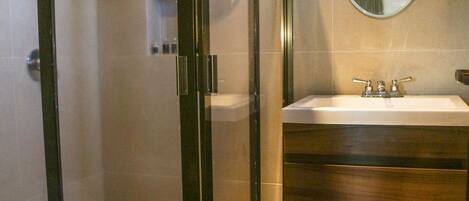 Um banheiro com chuveiro em gabinete de vidro, pia com espelho em cima e vaso sanitário.