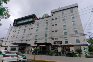 Um hotel com vários andares, com um logotipo 'SC' em destaque, um restaurante 'Voyage' e uma placa com o nome 'SC Hotel'.