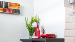 Pequena cozinha com dois banquinhos azuis, um eletrodoméstico vermelho e um vaso com planta.