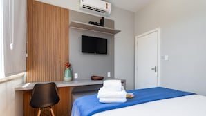 Quarto de hotel com cama, escrivaninha com cadeira, TV de tela plana e ar condicionado.