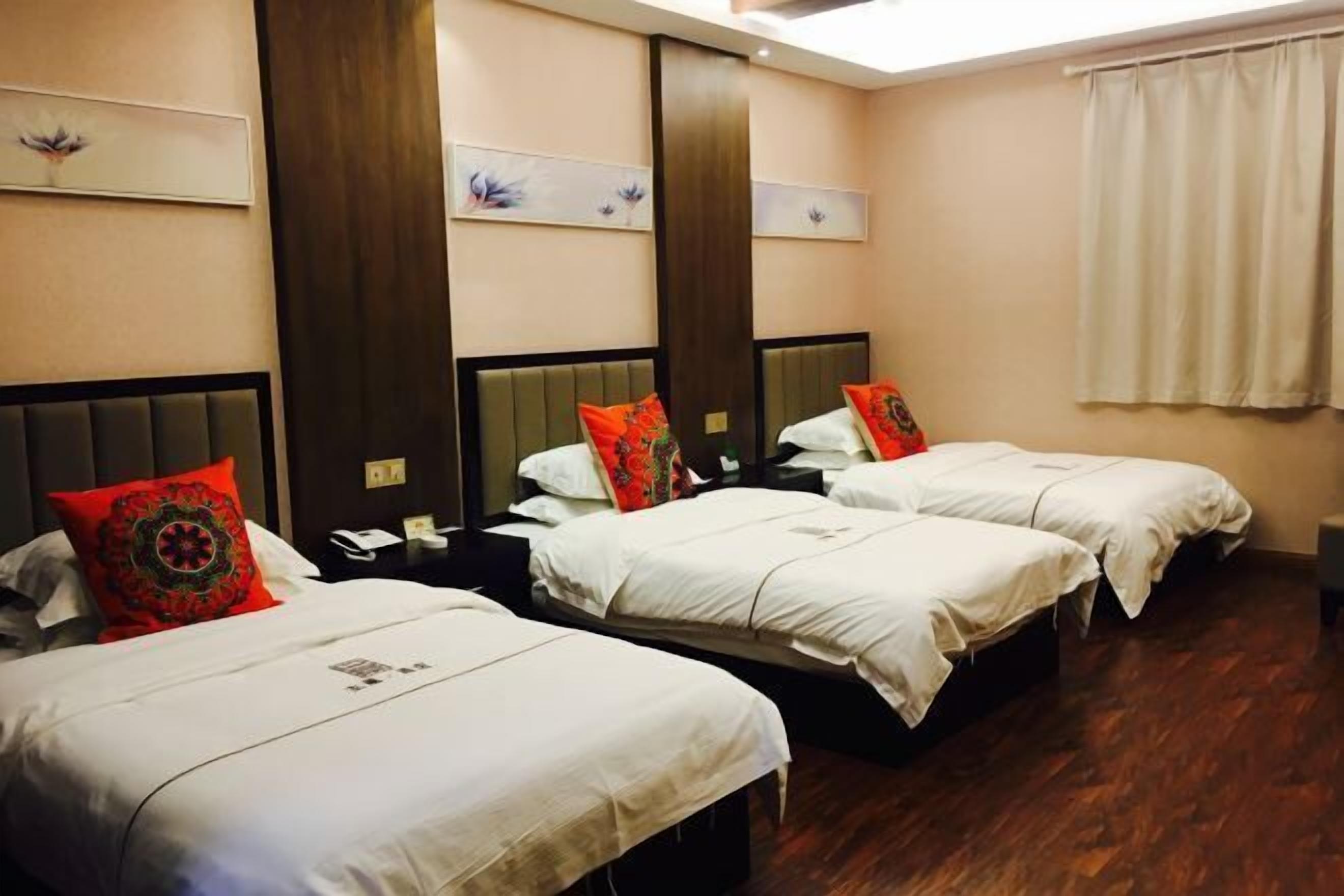 Quarto de hotel com três camas, cada uma com travesseiro e mesa de cabeceira.