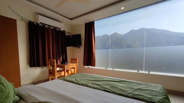 Quarto de hotel com cama, escrivaninha e uma grande janela com vista para as montanhas.