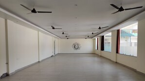 Um quarto espaçoso e vazio, com várias ventoinhas no teto, janelas amplas e um detalhe decorativo na parede.