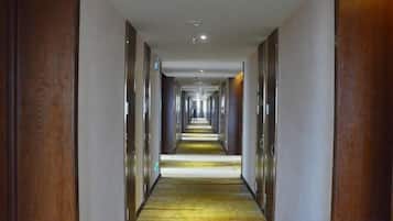 Corredor longo e estreito de hotel, com portas de ambos os lados, dando acesso a quartos individuais.
