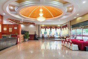 Um hall de hotel com balcão de recepção, escada e área de estar com mesas.