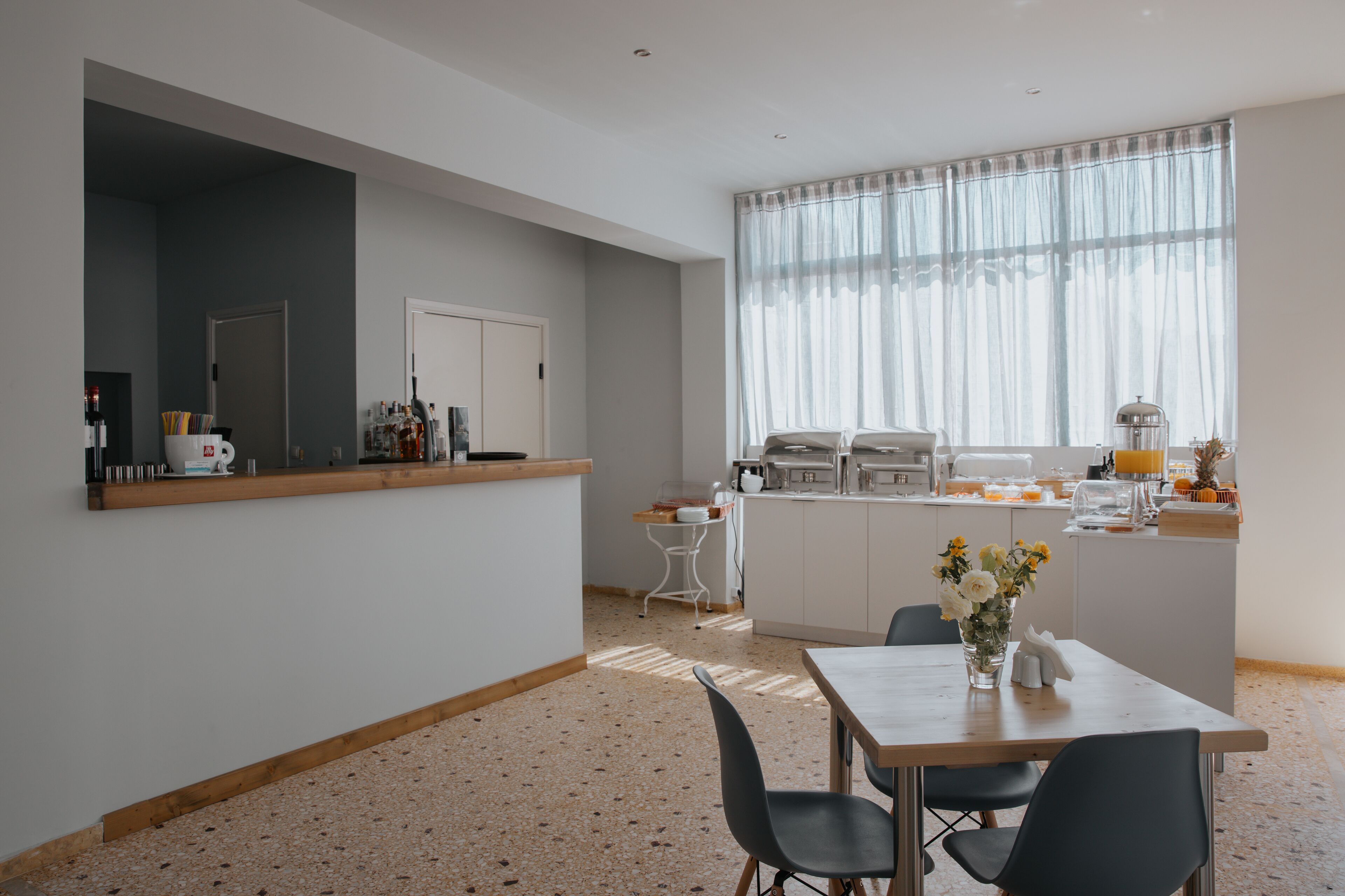 Uma cozinha moderna com uma ilha central, área de refeições com mesa e cadeiras, e uma grande janela com cortinas leves.