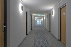 Corredor de hotel com portas em ambos os lados, carpete estampado e sinalização de saída verde.
