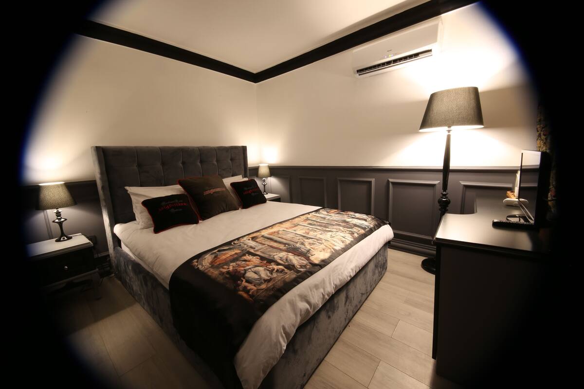 Quarto com uma cama grande, duas mesas de cabeceira, uma escrivaninha e um abajur.