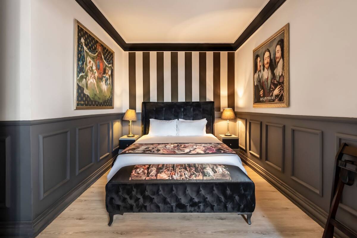 Quarto com uma cama grande, cabeceira escura e duas luminárias de cabeceira.