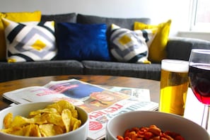 Uma mesa de jantar com um prato de batatas fritas, um prato de nozes, um copo de cerveja e um copo de vinho tinto.
