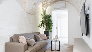 Uma sala de estar moderna com um sofá, uma mesinha, uma planta em vaso e uma TV fixada na parede.