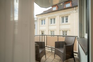 Uma varanda com cadeiras de vime, vista de um edifício com várias janelas e piso de azulejos.
