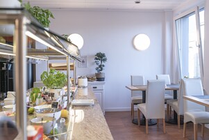 Uma cozinha moderna com uma bancada comprida, armários brancos e uma área de jantar com cadeiras e mesa brancos.