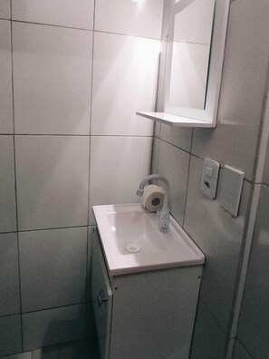 Um banheiro pequeno com pia branca, espelho e vaso sanitário.