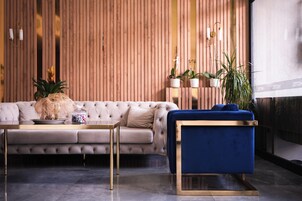 Uma sala de estar moderna com um sofá estofado, uma poltrona azul, uma mesa de centro de vidro e um painel de parede em madeira.