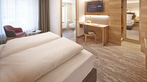 Quarto de hotel com uma cama grande, uma escrivaninha, uma cadeira, uma televisão e vista para o banheiro.