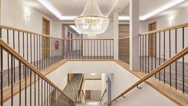 Uma escadaria imponente com um lustre, corrimãos de madeira e piso polido.