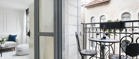 Varanda com mesa e cadeiras, um vaso de planta e vista para um edifício com janelas em arco.