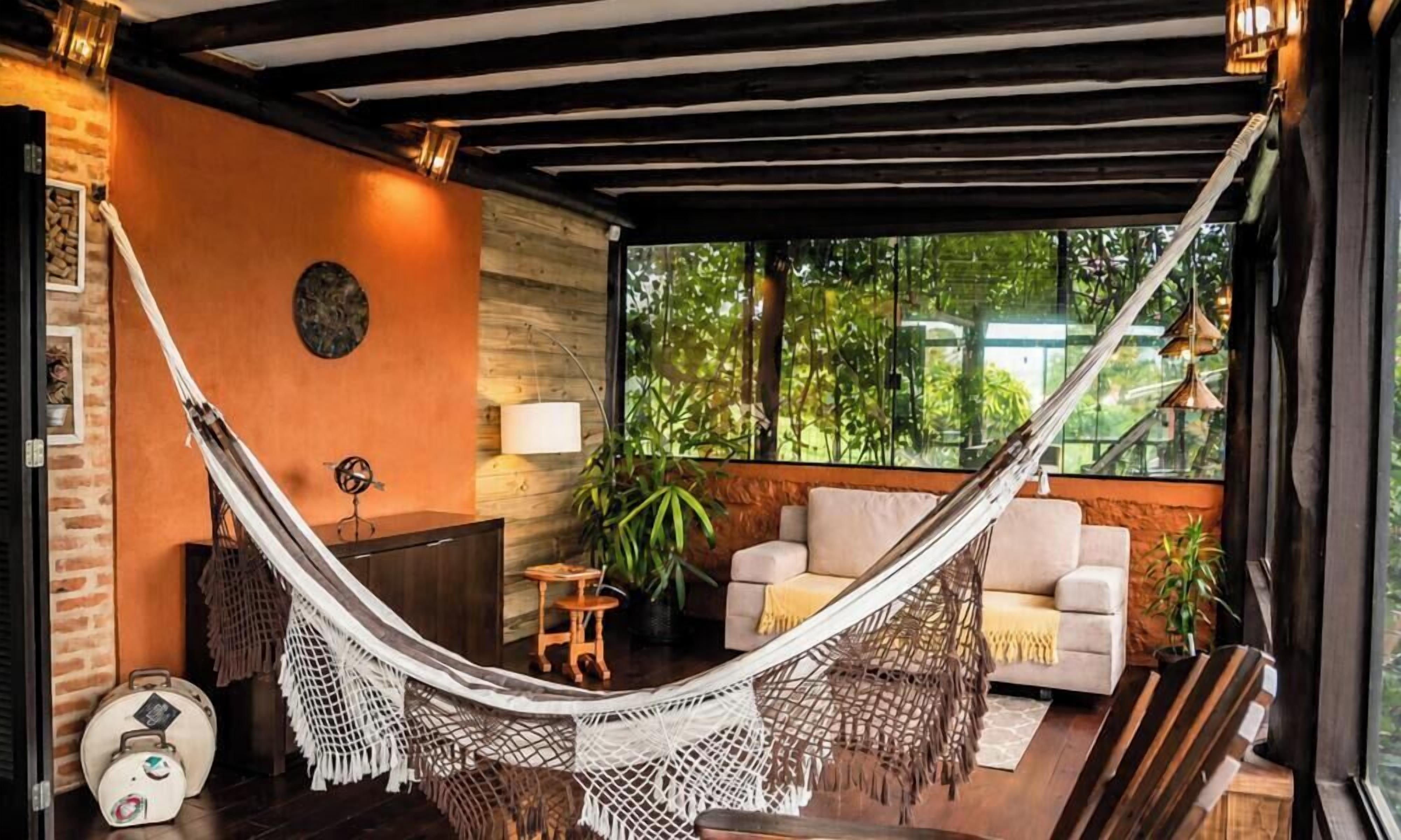 Uma rede em um quarto com parede de tijolos, teto de madeira e vista para o verde lá fora.