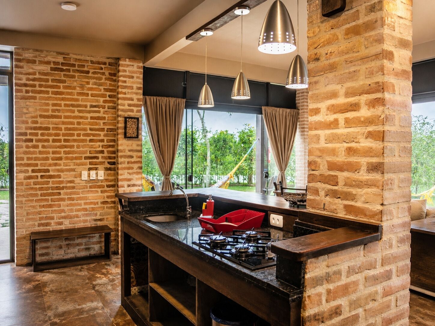Cozinha com parede de tijolos, fogão a gás e luminárias pendentes.