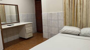 Quarto com cama, mesa de cabeceira com espelho, guarda-roupa de madeira e banheiro com piso em azulejo.