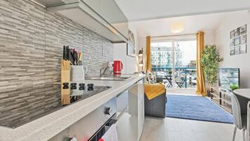 Uma cozinha moderna com fogão embutido, máquina de café e área de refeições com tapete azul e cortinas amarelas.