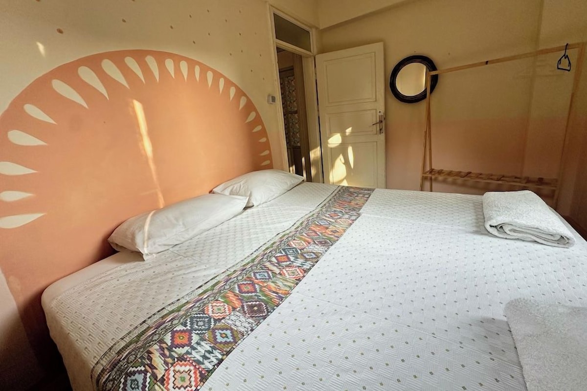 Quarto com cama, travesseiros, colcha estampada, porta e decoração circular na parede.