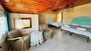 Quarto com duas camas, teto de madeira, uma pequena mesa com toalha florida e uma cadeira.