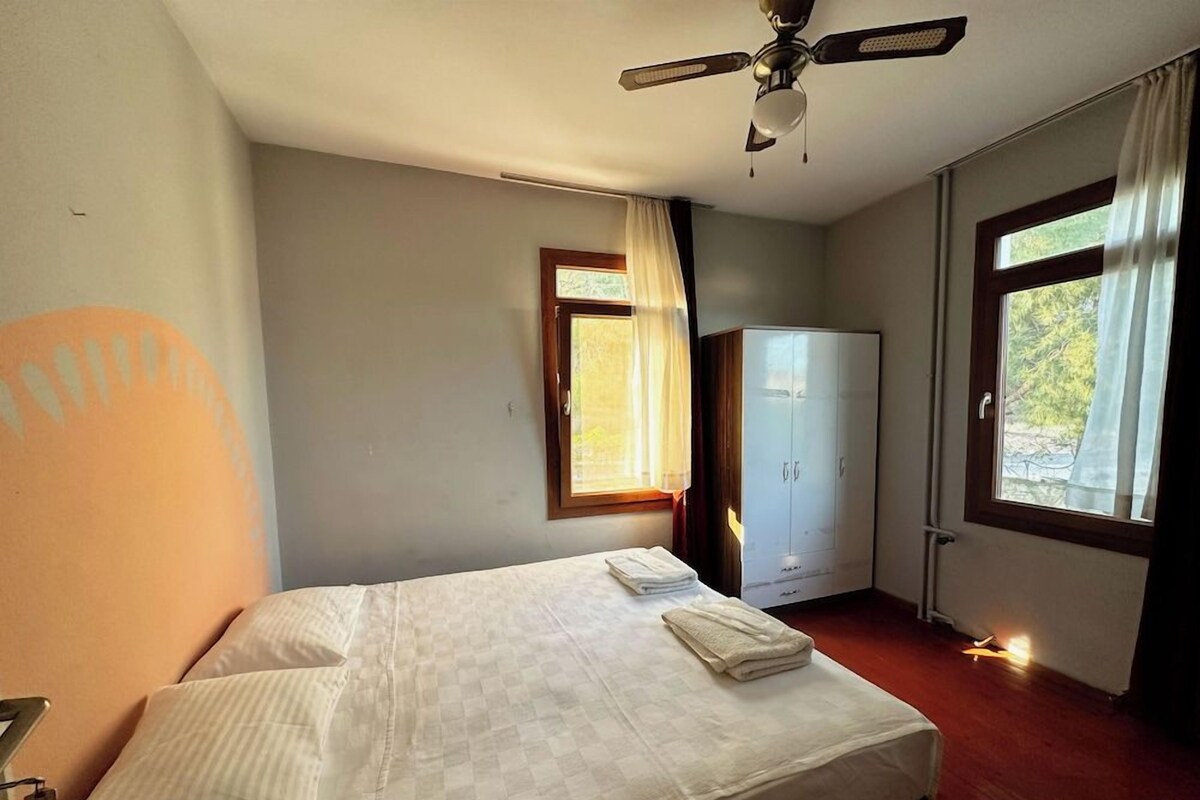 Quarto com cama, guarda-roupa, ventilador de teto e janela com cortinas.
