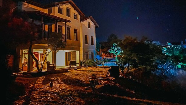 Um edifício de dois andares com varanda, entrada bem iluminada e área de jardim visível.