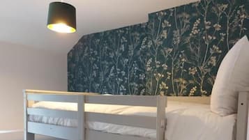 Quarto com beliche, papel de parede floral, mesa de cabeceira com abajur e janela.