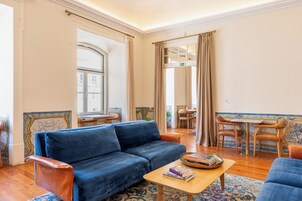 Uma sala de estar espaçosa com um sofá azul, mesa de centro de madeira e um espaço de refeições com cadeiras e mesa.