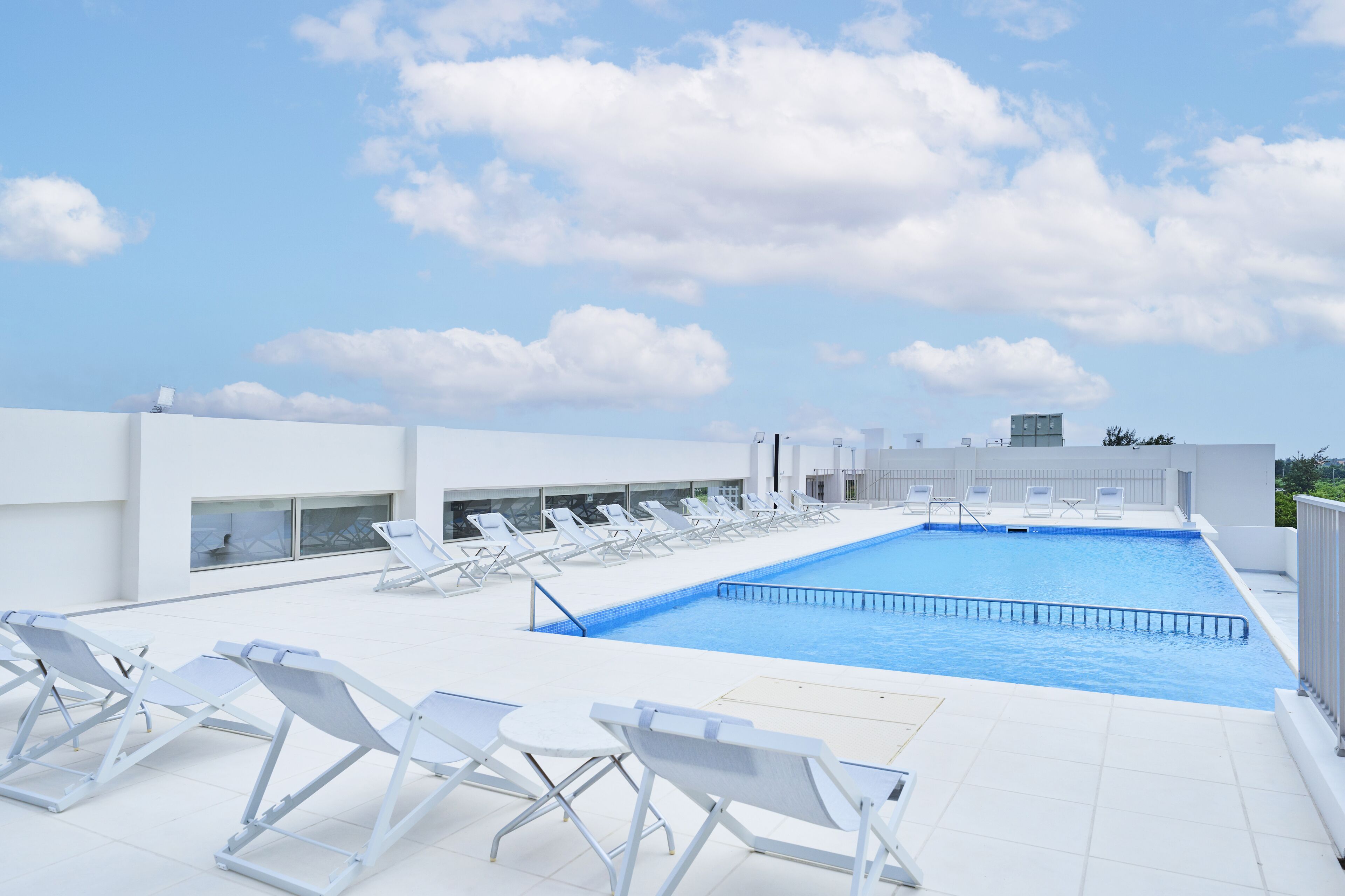 Piscina no terraço com cadeiras de sol brancas e céu azul límpido.