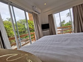 Quarto com cama grande, televisão e varanda com guarda-corpo de madeira.
